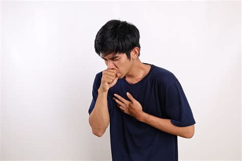 젊은 아시아 남자는 가슴을 잡고 주먹으로 기침을 했다 복사 공간이있는 흰색 배경에 격리 됨 기침하기에 대한 스톡 사진 및 기타