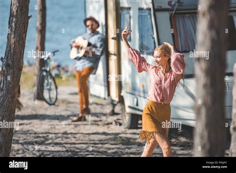 Young Hippie Woman Dancing While Man Playing Guitar Near Trailer Stock