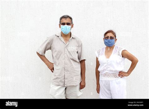 Older Latino Couple With Protective Face Masks On White Wall Background