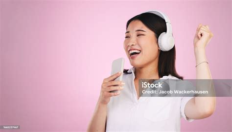 헤드폰 노래 그리고 음악 재생 목록 또는 라디오를 듣는 스튜디오에서 전화기를 가진 여성 행복하고 미소를 짓고 젊은 아시아 여성 모델이 분홍색 배경의 노래에 맞춰 핸드폰