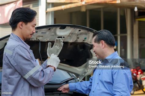 안전을 위해 장갑을 끼고 후드가 열린 차량 근처에서 고객에게 자동차 수리 문제를 설명하는 정비사 소규모 자동차 수리 업체에서 명확한 의사 소통과 전문성을 강조합니다 2명에