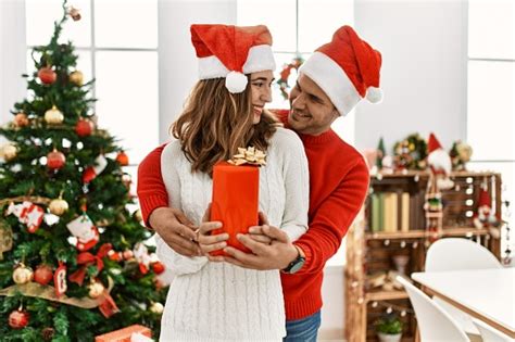 집에서 선물을 들고 크리스마스 모자를 쓰고 젊은 히스패닉 부부 12월에 대한 스톡 사진 및 기타 이미지 12월 25 29세 2명 Istock