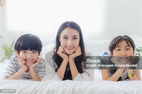 아늑한 집에서 사랑스러운 행복한 아시아 가족 웃는 어머니 아들과 딸은 침실에서 함께 휴식을 취하고 장난을 치는 것을 즐깁니다