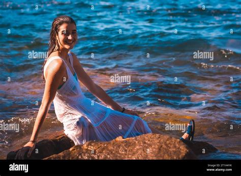 A Young Caucasian Girl Smiling In A Wet White Dress Sitting On A Rock