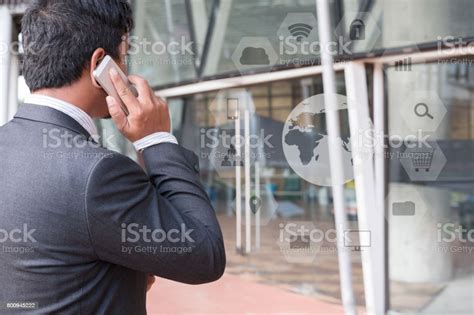 외부 건물에 서 있는 동안 스마트 폰 얘기 한 벌에서 사업가 통신 및 인터넷 아이콘을 가진 현대 사무실 복도에서 작업에 대 한 휴대 전화를 사용 하 여 젊은 아시아 남자