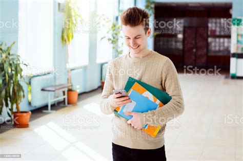 화창한 날에 소셜 미디어를 통해 친구들과 문자 메시지를 보내는 대학 캠퍼스에 서있는 스마트 폰과 코스 책을 가진 쾌활한 백인 학생 18 19세에 대한 스톡 사진 및 기타