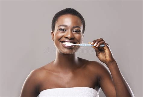 Portrait Of Beautiful African Woman Brushing Teeth On Gray Background