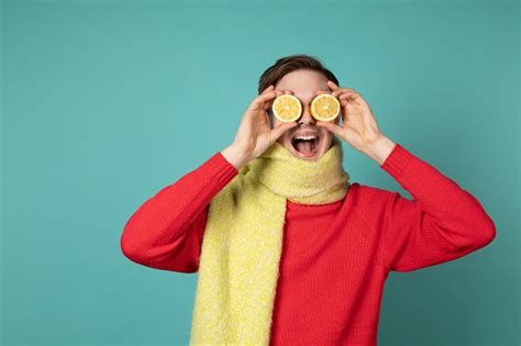 빨간 스웨터에 있는 잘생긴 젊은 남자와 손에 있는 감귤 류 과일의 Halfs를 들고 노란 스카프 그녀의 눈을 덮고 가을에 대한