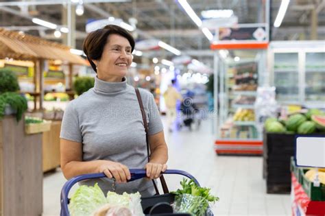 Mature Woman Standing In Grocery Store With Groceries In Cart Stock