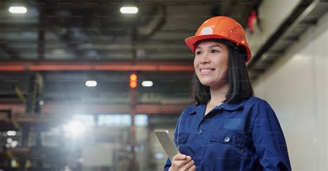 Cheerful Young Female Wngineer With Touchpad Standing In Workshop Of Industrial Plant While