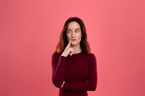 분홍색 배경 위에 고립 된 아름다운 젊은 아가씨는 손가락으로 입 가까이에서 사려 깊은 제스처를 표현했습니다 갈색 머리에 대한