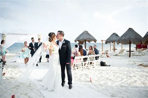 A Bride And Groom Kissing On The Beach In Front Of Their Wedding Party
