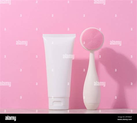 White Plastic Tube And A Massage Brush For Facial Cleansing On A Pink