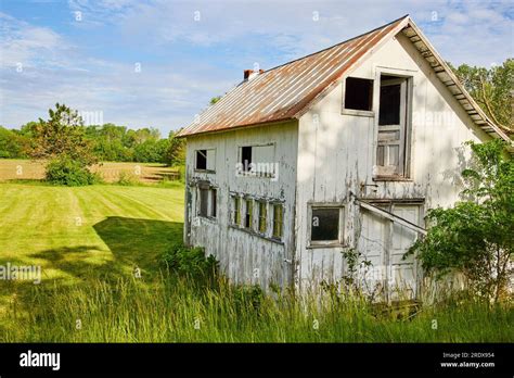 Abandoned Farm House In Grassy Field Near Farmland With Busted Windows