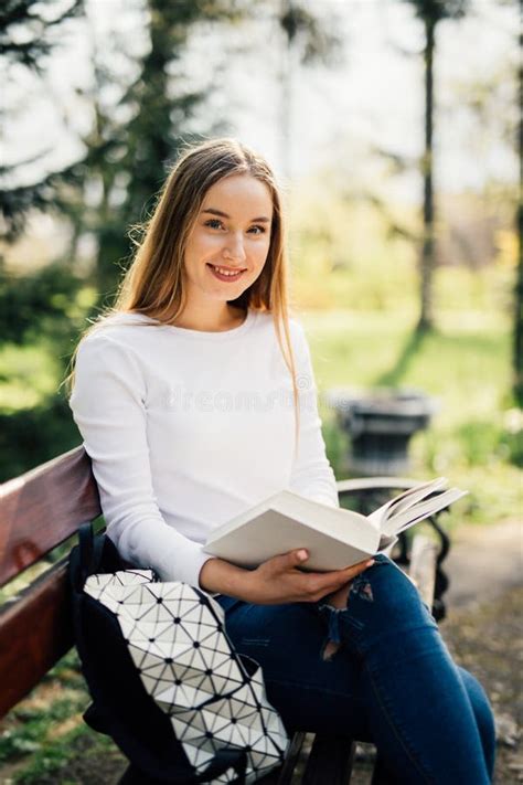 La Muchacha Del Estudiante Que Se Sienta En Un Banco Leyendo Un Libro En Parque Imagen De