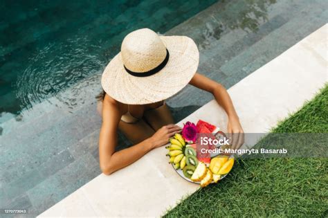 발리의 고급 빌라에서 수영장 근처에서 휴식을 취하고 과일을 먹는 소녀 발리 소순다 열도에 대한 스톡 사진 및 기타 이미지 발리 소순다 열도 여자 해변 Istock