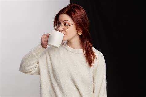 뜨거운 음료가 활기를 띠고 있습니다 차 또는 커피 한 잔을 손에 들고 있는 빨간 머리 여자 큰 안경에 반쯤 흰색과 검은 색