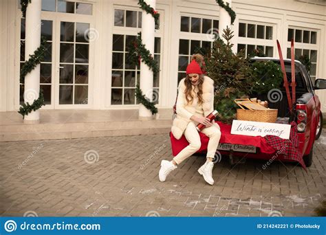 Attractive Woman In White Fur Coat And Red Hat Sits On Her Red Car