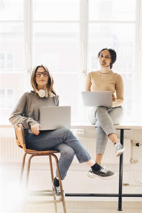Portrait Of Female Computer Programmers With Laptops Sitting At Desk In Office Stock Photo