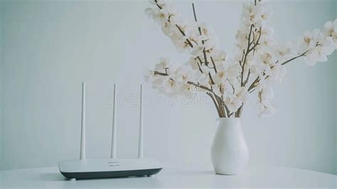 A White Router Sits Beside A Vase Of Flowering Branches On A Clean