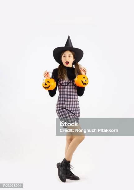 할로윈 테마 검은 드레스와 부츠를 입은 젊은 아시아 여성은 흰색 배경에 오렌지색 호박 양동이와 등불을 들고 들고 마녀 모자를
