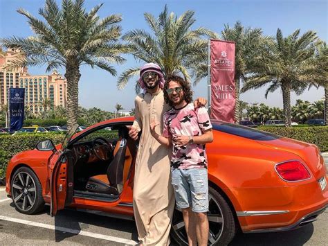 Two Men Standing Next To An Orange Car With Its Doors Open And Palm