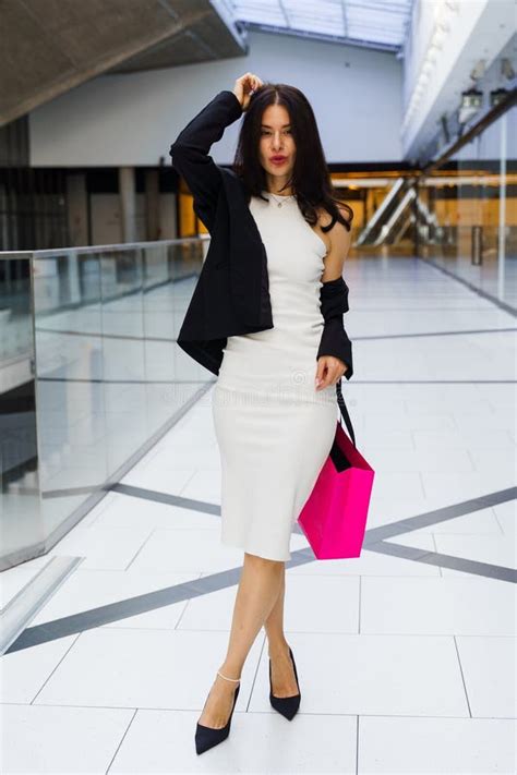 Flirtatious Woman In White Dress And Black Jacket Is Walking In City