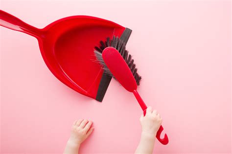 밝은 분홍색 바닥 배경에 빨간 빗자루와 먼지 팬을 가지고 노는 아기 손 보육원에서 정기적인 청소 근접 촬영 관점 샷 하향 보기