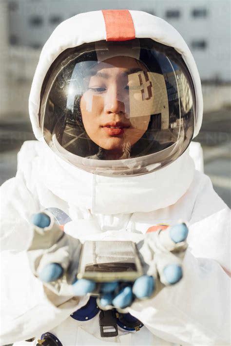 Female Astronaut In Space Suit Looking At Smart Phone In Hands During
