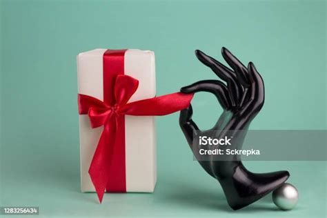 마네킹 여성 플라스틱 핸드는 선물 상자의 빨간 활을 들고 있습니다 크리스마스와 새해 인사말 카드 또는 배너를위한 미니멀 한 개념