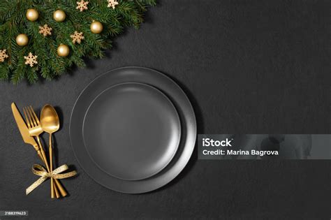 검은 배경에 황금 칼 붙이 축제 장식 및 전나무 가지가 있는 빈 검은 접시 크리스마스 또는 새해 저녁 식사 텍스트를 위한 공간입니다 평면도 평면도 0명에 대한 스톡 사진 및
