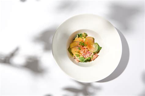 거친 그림자가있는 흰색 테이블에 게 고기 에스푸마 소스 및 양상추를 곁들인 우아한 샐러드 여름 메뉴에 게와 크림 소스를 곁들인 그린 샐러드 미적 음식 해산물 전채 갈고리