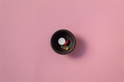 흰색 빨간색 및 노란색 비타민 알약은 텍스트를위한 공간이있는 분홍색 배경에 어두운 세라믹 그릇에 있습니다 의학과 건강 0명에