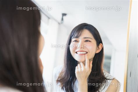姿鏡の前で鏡に映る自分の歯の調子を眺めて笑顔になる20代〜30代の日本人女性 （人物）の写真素材 215687224 イメージマート