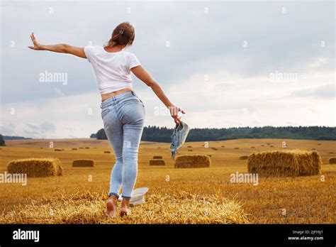 Barefoot Girlwith Sneakers In Hand Stands On A Haystack On A Bale In