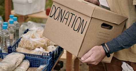 포장된 기부 상자를 들고 있는 남성 자원봉사자는 무료 음식이 있는 테이블 옆에 서 있다 사진 Unsplash의 상자 이미지