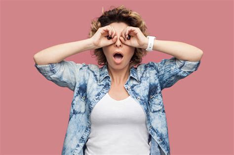 쌍안경 제스처 와 눈과 깜짝 놀란 얼굴카메라를보고 서 파란색 셔츠에 곱슬 머리와 충격 재미 젊은 여자의 초상화 갈색 머리에 대한 스톡 사진 및 기타 이미지 Istock