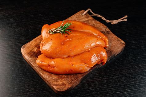 어두운 배경의 나무 부엌 보드에 빨간 소스에 생 절인 치킨 필레와 요리를위한 향신료가 있습니다 공간을 복사합니다 식이 닭고기