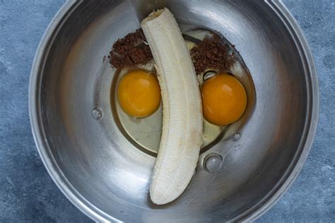 바나나 팬케이크를 만들기위한 계란 잘 익은 바나나 및 코코아 가루가 든 금속 그릇 얼굴 모양의 재미있는 음식 가루로 빻은에 대한