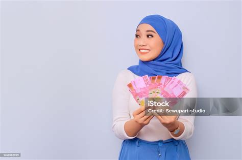 웃고 있는 젊은 아름다운 아시아 무슬림 여성이 돈 지폐를 들고 흰색 배경 위에 격리된 복사 공간을 바라보고 있다 20 24세에 대한 스톡 사진 및 기타 이미지 Istock