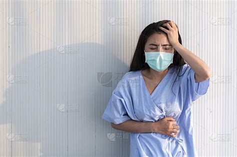 女患者戴口罩，靠墙站立，疼痛、抑郁。年轻女性从手术中恢复。年轻的亚洲女病人在医院里。病人的沮丧和悲伤