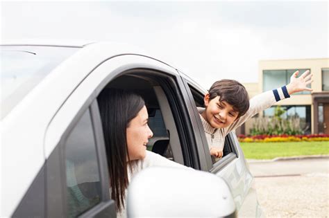 엄마와 아들은 회색 차 안으로 들어가서 아이가 파일럿 창에서 그를 보기 위해 머리를 찌르는 어머니를 보면서 팔을 뻗어 뒤쪽 창문을 내보며 보입니다 2명에 대한 스톡 사진 및