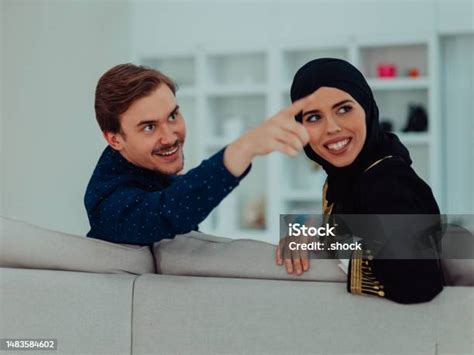 현대 가정에서 라마단 한 달 동안 소파에 앉아 함께 Tv를 시청하는 이슬람 히잡 옷을 입은 젊은 무슬림 부부 여성 여자에 대한