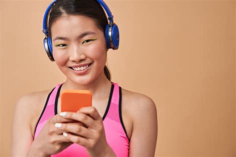스마트폰을 들고 카메라를 향해 미소짓는 헤드폰을 착용한 여성 20 24세에 대한 스톡 사진 및 기타 이미지 20 24세