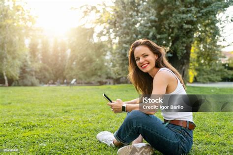도시 공원에서 휴식을 취하고 카메라를 보며 미소 짓는 휴대 전화를 가진 도시 여성 25 29세에 대한 스톡 사진 및 기타 이미지 25 29세 30 39세 35 39세