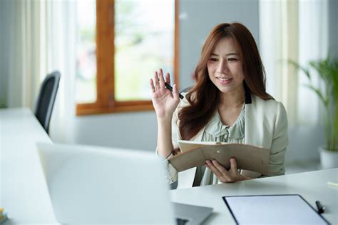 노트북을 사용하는 아시아 은행 직원의 초상화 사무실의 책상에서 예산 서류 작업을 수행하는 팀원들과 화상 회의 가정 생활에 대한