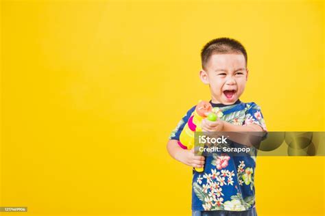 초상화 행복 한 아시아 귀여운 어린 아이 소년 미소 서 너무 행복 입고 꽃 셔츠를 입고 송크란 축제 날 들고 물 총 복사 공간 노란색 배경에 스튜디오 샷 물에 대한 스톡
