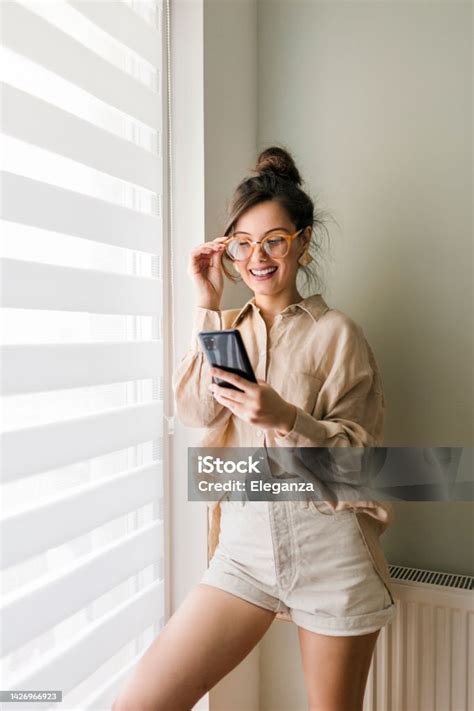 스마트 폰을 사용하고 창문 옆에 서있는 아름다운 젊은 여성 휴대전화에 대한 스톡 사진 및 기타 이미지 휴대전화 사람들 한 사람 Istock