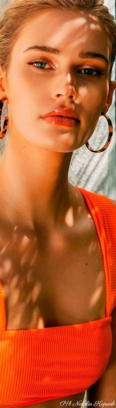 A Woman In An Orange Top With Large Hoop Earrings On Her Head And One