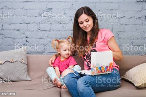 젊은 엄마와 딸의 2 년 오래 된 금발 소파 실내에 앉아 밝은 인쇄와 흰색 노트북 컴퓨터 노트북을 사용 가족에 대한 스톡 사진